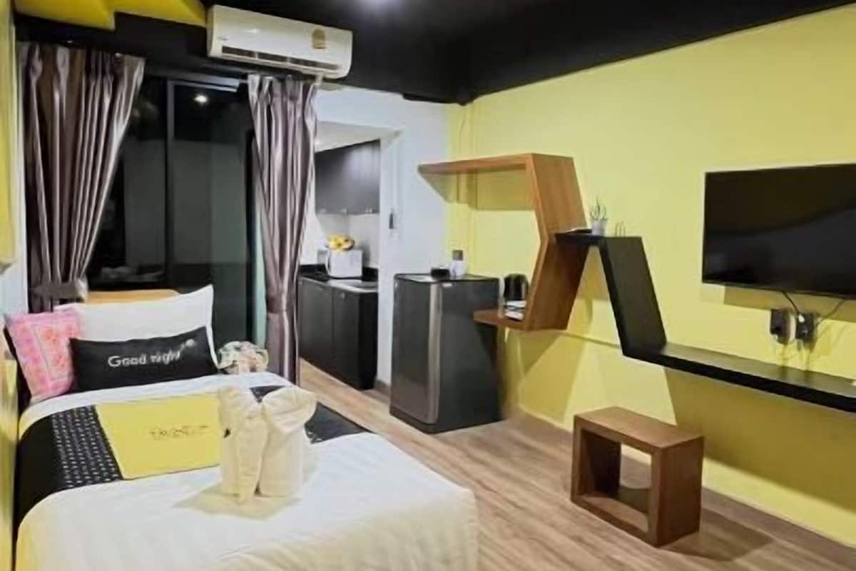 Quarto de hotel moderno com teto curvo, cama com edredom branco, mesa de cabeceira pequena, televisão fixada na parede e janela com cortinas.