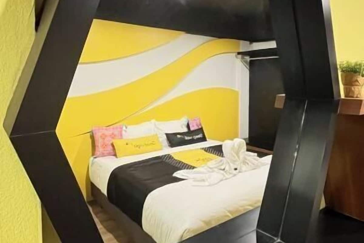 Quarto com uma cama, uma estrutura geométrica preta e uma parede amarela.