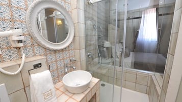 Casa de banho com espelho redondo, lavatório com toalha e zona de duche.