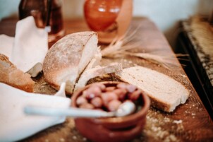Uma mesa de madeira com pão fatiado, uma tigela de feijão e uma colher.