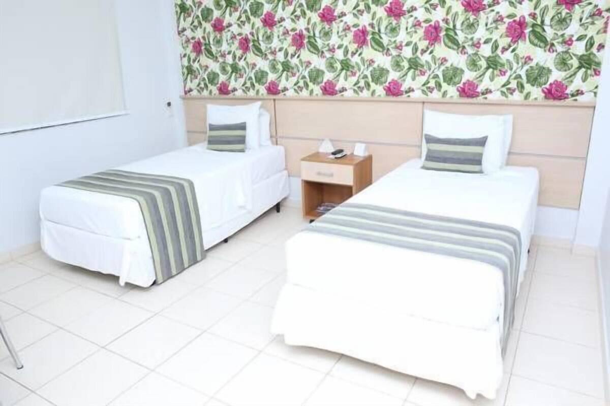 Quarto de hotel com duas camas, uma mesa de cabeceira e um papel de parede floral.