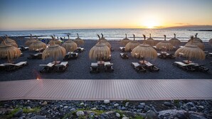Restaurante à beira-mar com guarda-sóis de palha e mesas de madeira, com vista para o oceano.