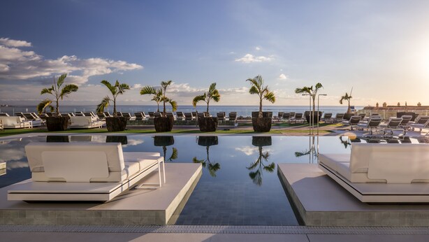 Piscina infinita no terraço com espreguiçadeiras e palmeiras, com vista para o oceano.