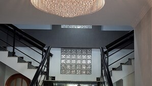 Uma imponente escadaria com um lustre, uma porta de madeira e uma parede com padrão quadriculado.