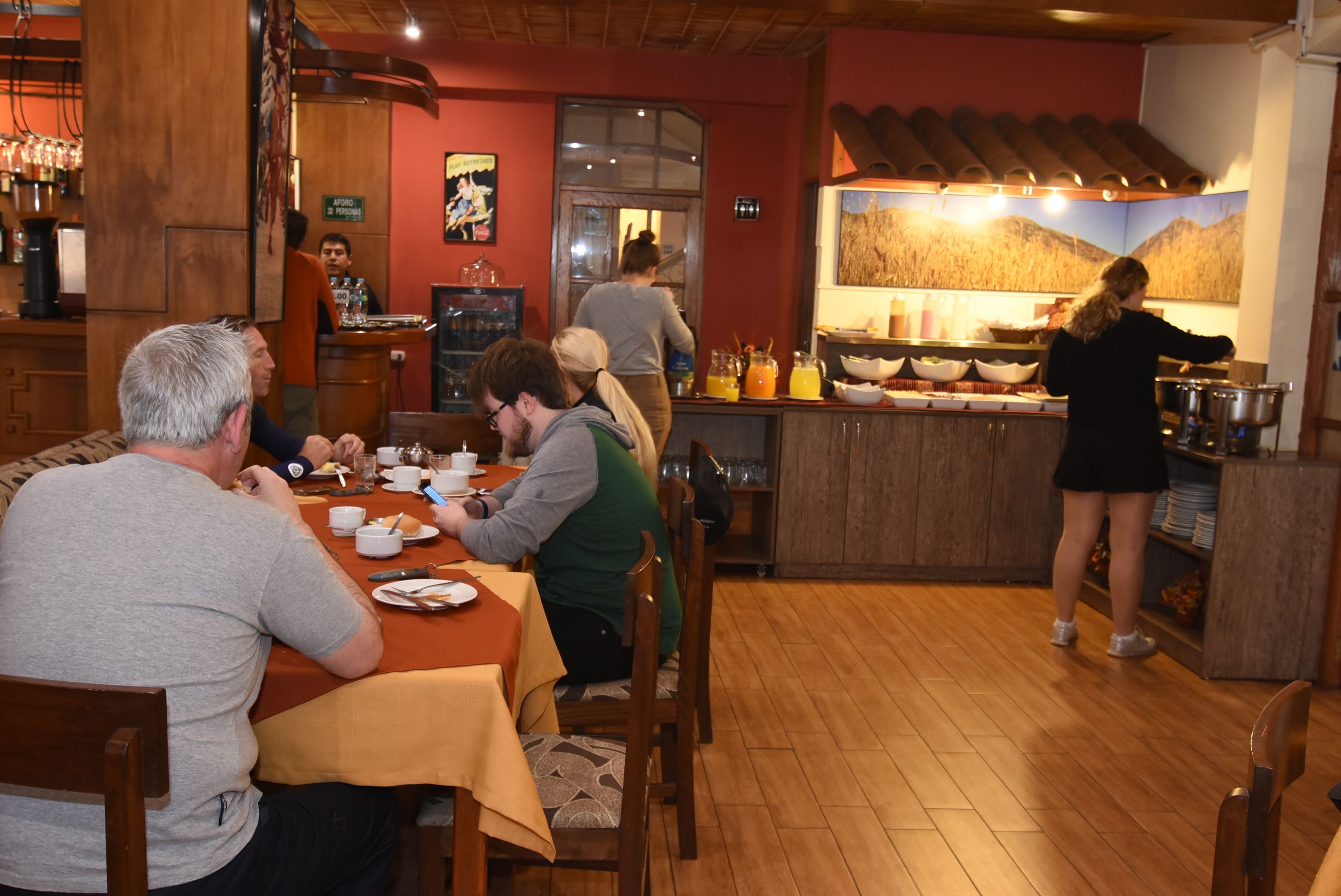 Restaurante com interiores em madeira, área de bar e balcão onde um atendente prepara alimentos.