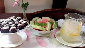 Uma mesa com um prato de brownies, uma tigela de melancia em fatias e um jarro de limonada.