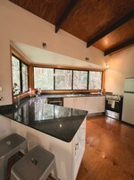 Cozinha com uma ilha grande, vigas de madeira no teto e vista para uma floresta através de amplas janelas.