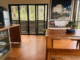 Cozinha moderna com bancada de madeira, mesa de jantar e vista para um jardim através de grandes portas deslizantes.