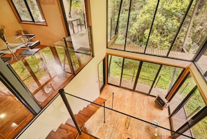 Interior moderno com escada de madeira, janelas amplas e vista para um jardim.