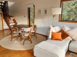 Uma sala de estar com uma mesa de madeira redonda, sofá branco e escada.