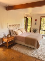 Quarto com cama, mesa de cabeceira, janela e vista para árvores.