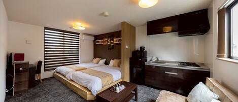 Quarto de hotel compacto com cama, escrivaninha, cozinha compacta e sofá.