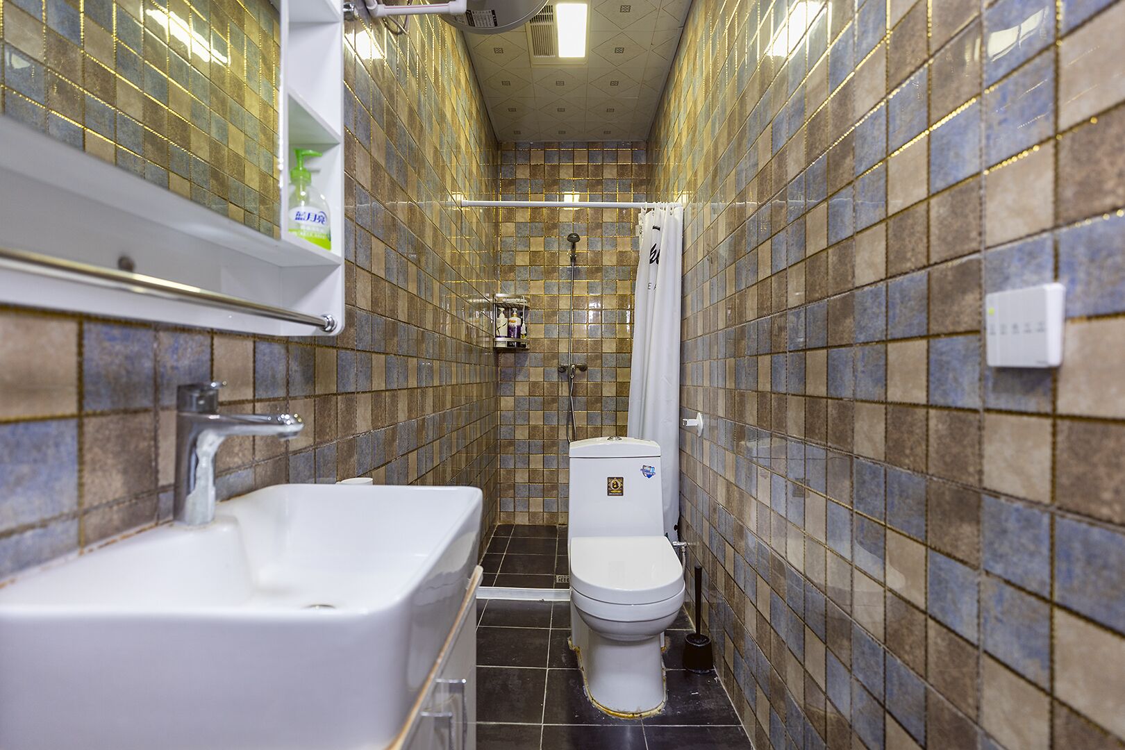 Casa de banho com lavatório, sanita e chuveiro brancos. As paredes estão revestidas com azulejos castanhos e bege.
