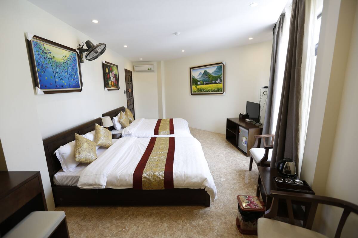 Quarto de hotel com uma cama grande, uma mesa, uma cadeira, uma TV e obras de arte nas paredes.