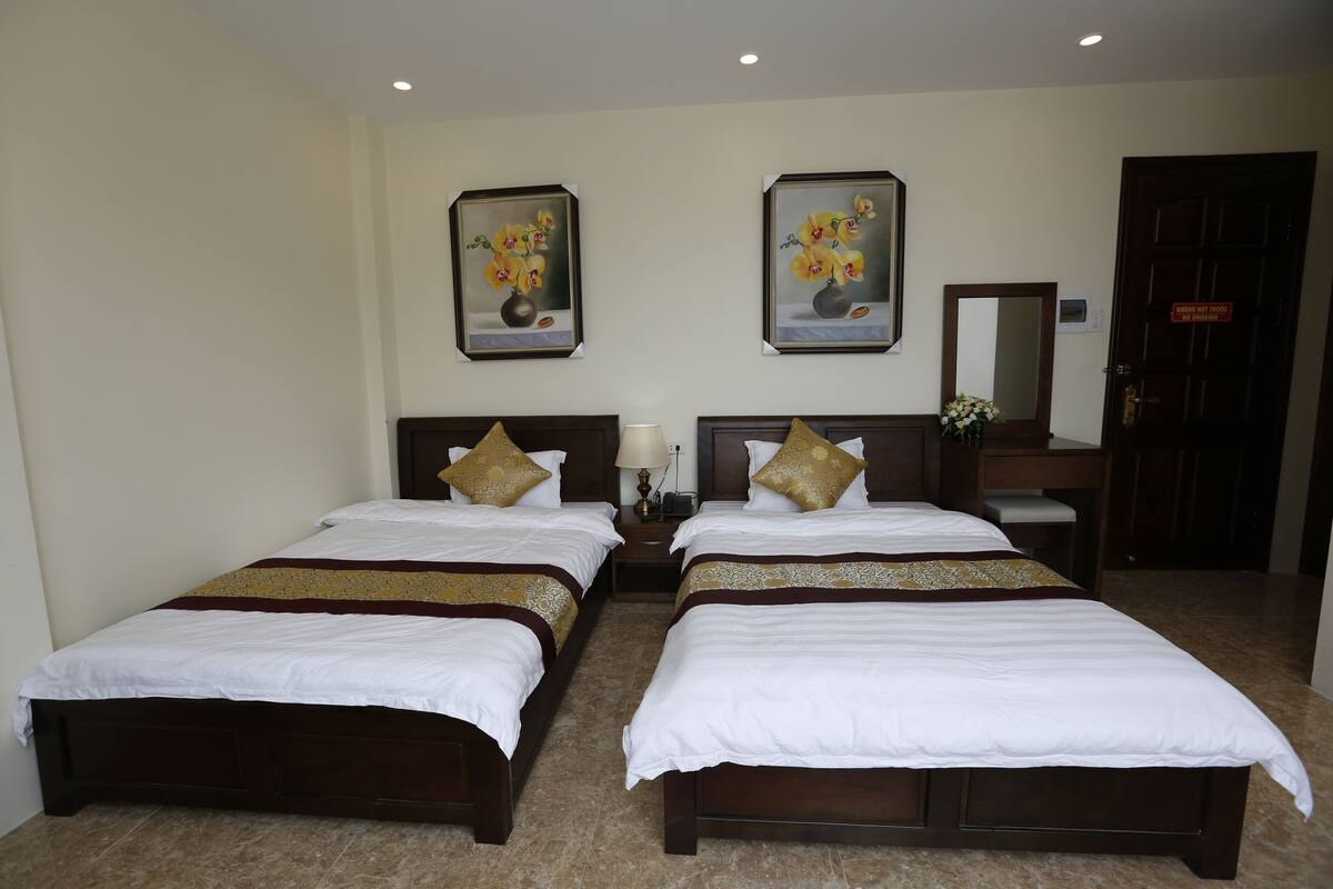Quarto de hotel com duas camas, uma mesinha de cabeceira, um espelho e duas pinturas na parede.
