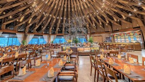 Um restaurante com teto alto de madeira e mesas preparadas com guardanapos e talheres.