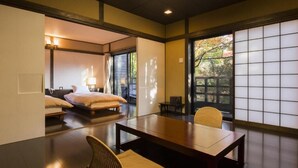 Quarto japonês tradicional com piso de tatame, uma mesa baixa e uma porta deslizante que dá acesso a um espaço para dormir com futons.