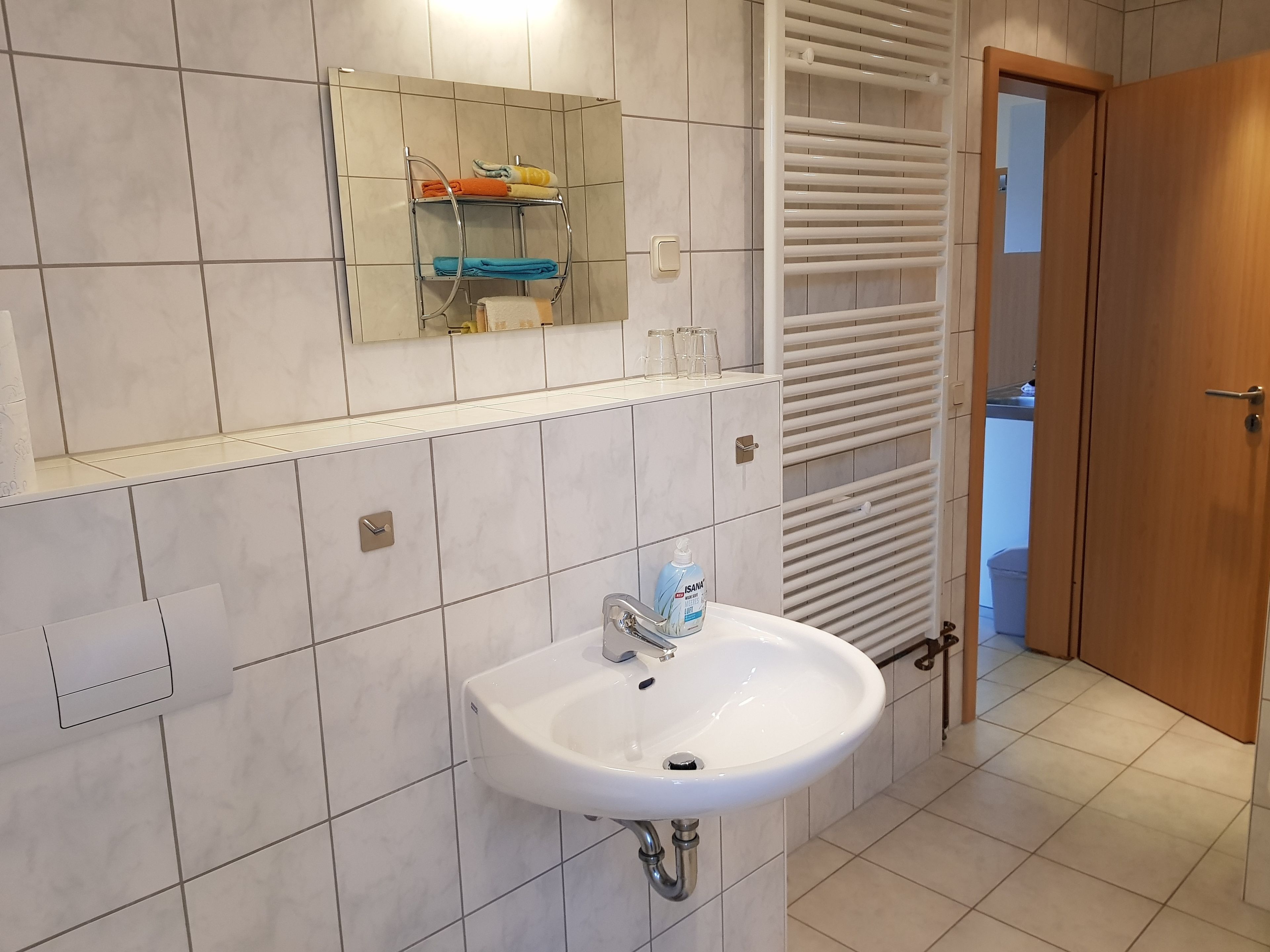 Uma casa de banho com uma pia branca, um espelho, um porta-toalhas e um aquecedor.