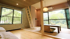 Quarto com piso de madeira, janelas amplas, escada, mesa com almofadas e ar condicionado.