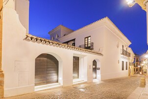Um edifício histórico com rua de paralelepípedos, paredes brancas e uma varanda com grades de ferro forjado.