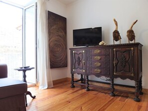 Quarto com piso de madeira, um armário de madeira escura com puxadores decorativos, uma TV de tela plana em cima e uma grande pintura abstrata na parede.