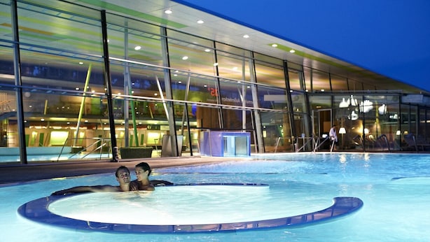 Piscina com área de hidromassagem, rodeada por um edifício moderno com grandes janelas.