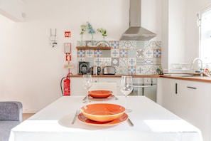 Cozinha moderna com armários brancos, painel de azulejos e mesa com pratos laranja e copos de vinho.