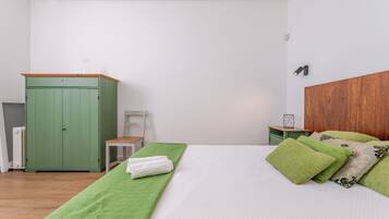 Quarto com cama, colcha verde, almofadas brancas, guarda-roupa verde, cabeceira de madeira e mesa de cabeceira com abajur.