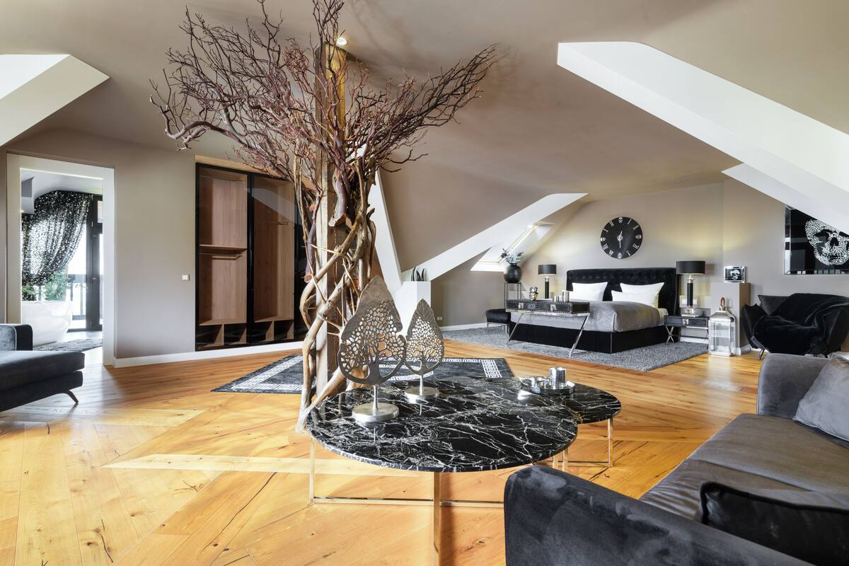 Um amplo loft com pé direito alto, uma mesa central de mármore preto, um sofá moderno e uma escultura de árvore decorativa.