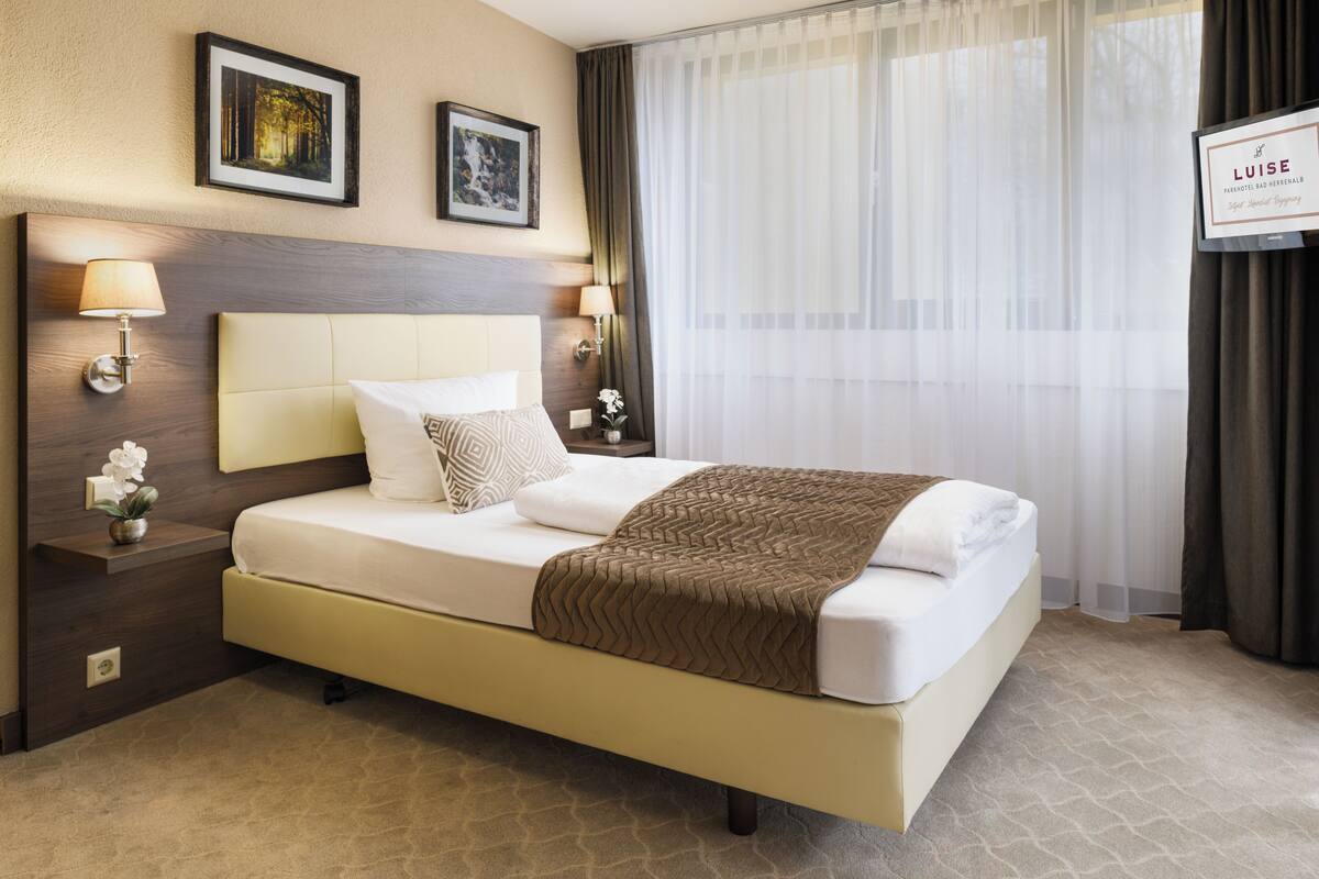 Quarto de hotel com uma cama, mesas de cabeceira, abajures e quadros nas paredes.
