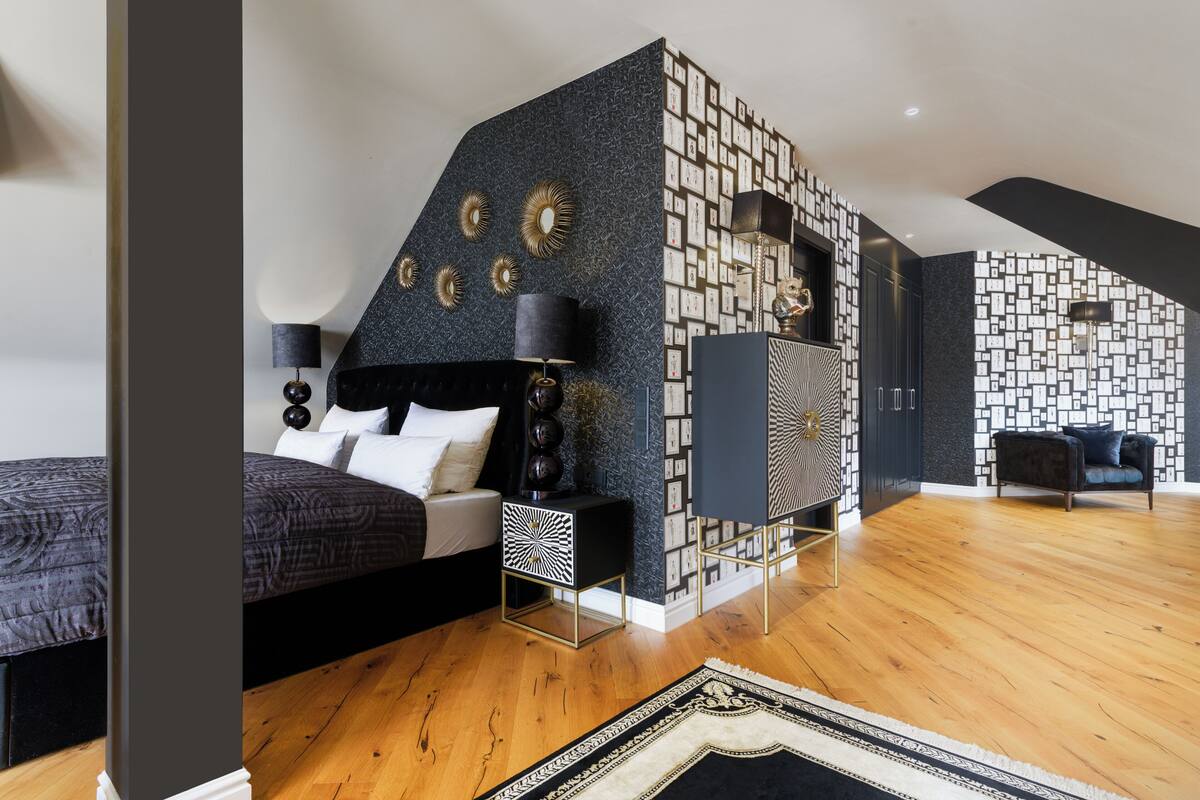 Quarto moderno com uma cama grande, uma mesa de cabeceira, cômoda e um espaço de estar com uma cadeira e uma mesa pequena.