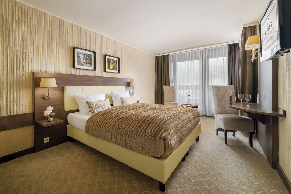 Quarto de hotel com uma cama grande, uma escrivaninha com cadeira, televisão e janela com cortinas.