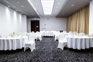 Uma sala de conferências com várias mesas redondas, cadeiras brancas e um tapete preto estampado.