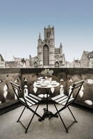 Mesa com cadeiras em um terraço, com vista para uma igreja histórica com torres pontiagudas.