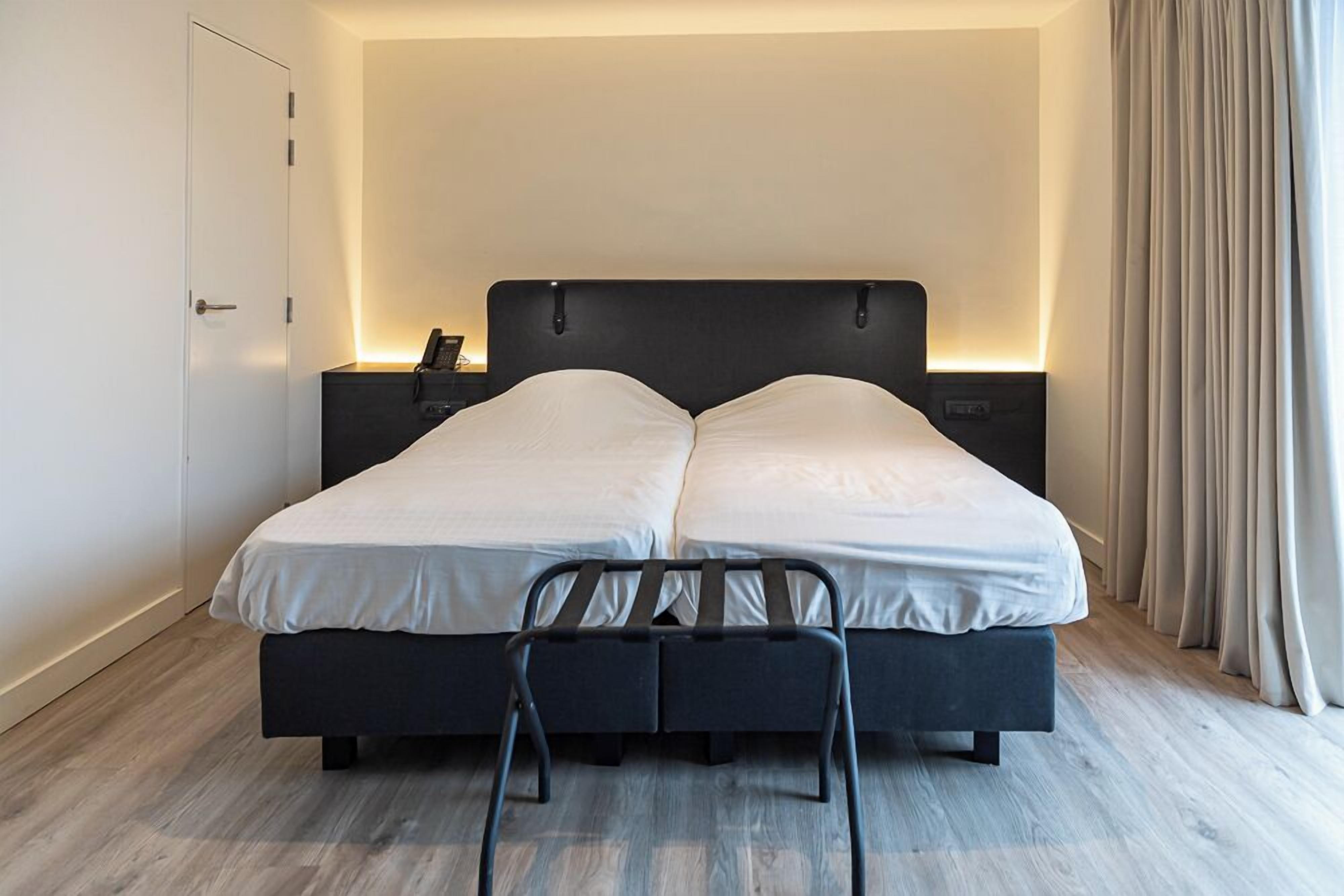 Quarto moderno com cama de casal, mesas de cabeceira e criado-mudo.