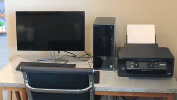 Uma escrivaninha com computador, monitor, teclado e impressora.