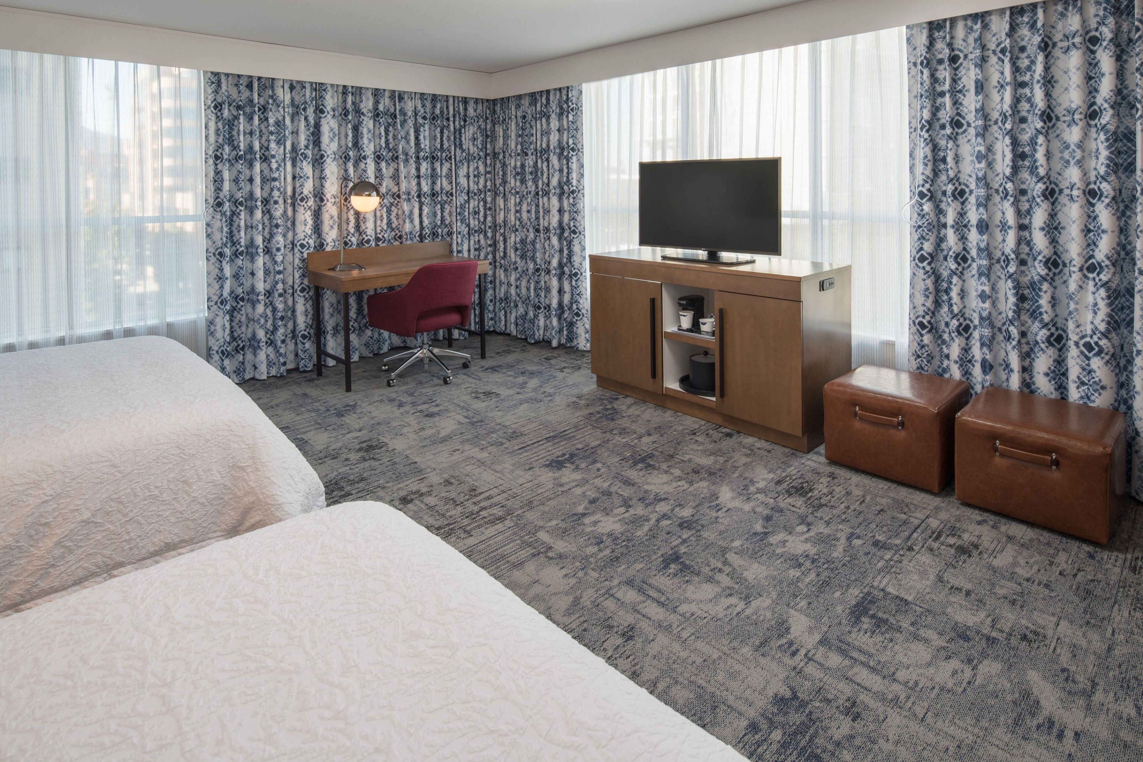 Quarto de hotel com cama, secretária, cadeira, televisão e armários.