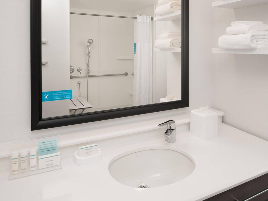 Casa de banho de hotel com lavatório branco, espelho e porta-toalhas.