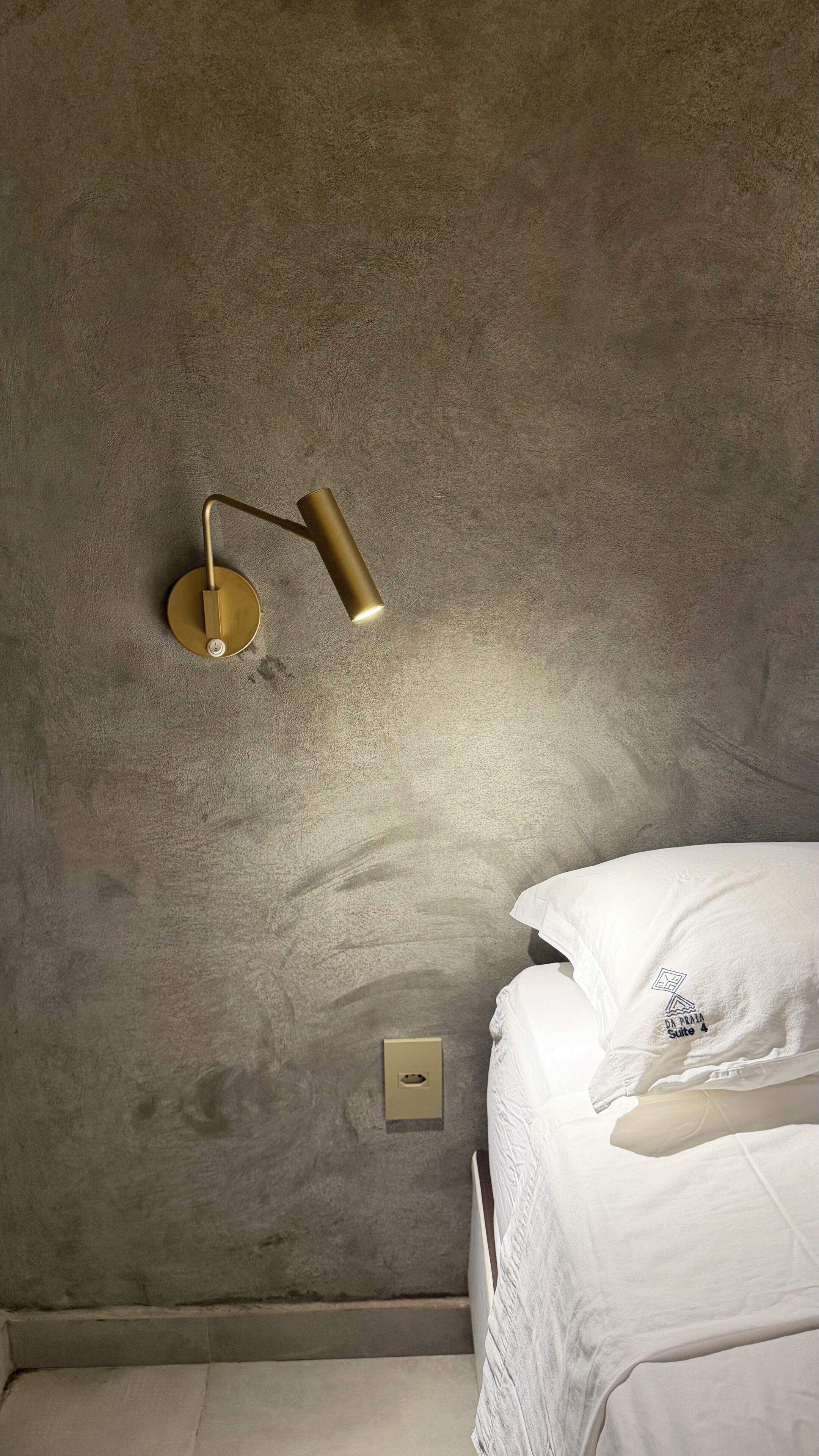 Quarto com uma cama, uma luminária na parede e um interruptor.