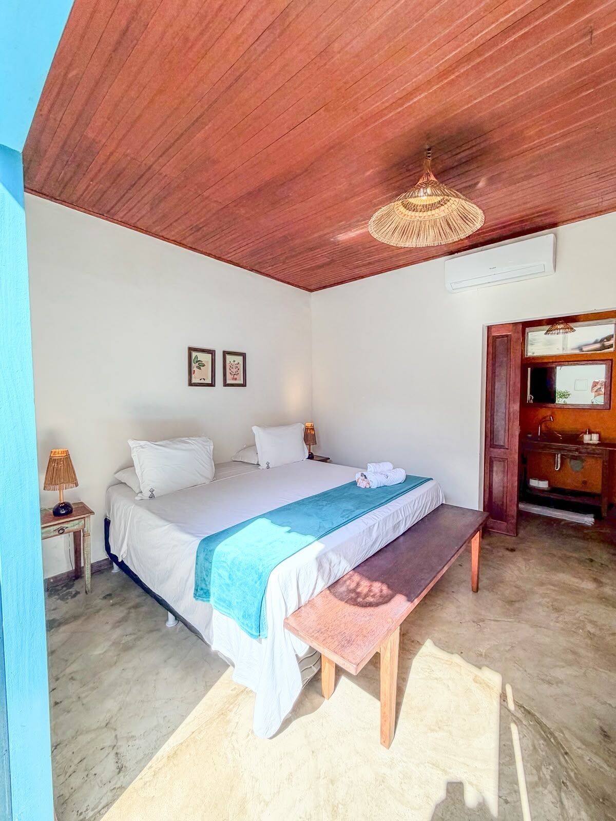 Quarto com cama, mesas de cabeceira, um banco, luminária pendente e guarda-roupa de madeira.