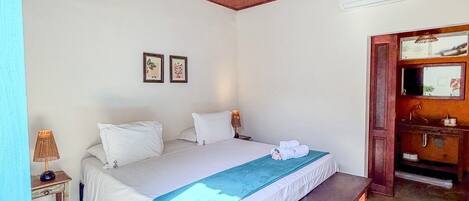 Quarto com cama, mesas de cabeceira, um banco, luminária pendente e guarda-roupa de madeira.