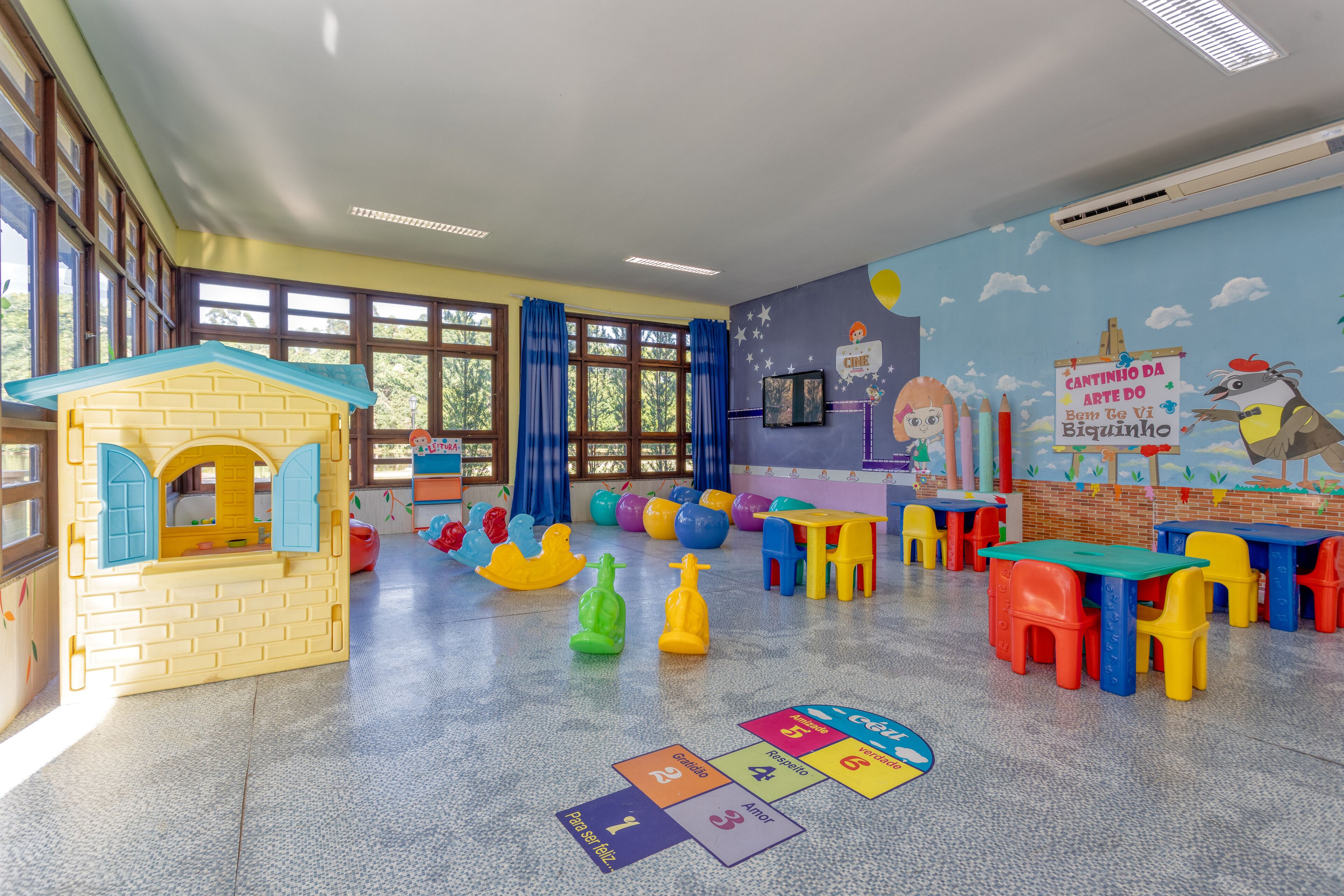 Uma sala de aula com estruturas lúdicas coloridas, mesas e cartazes educativos.