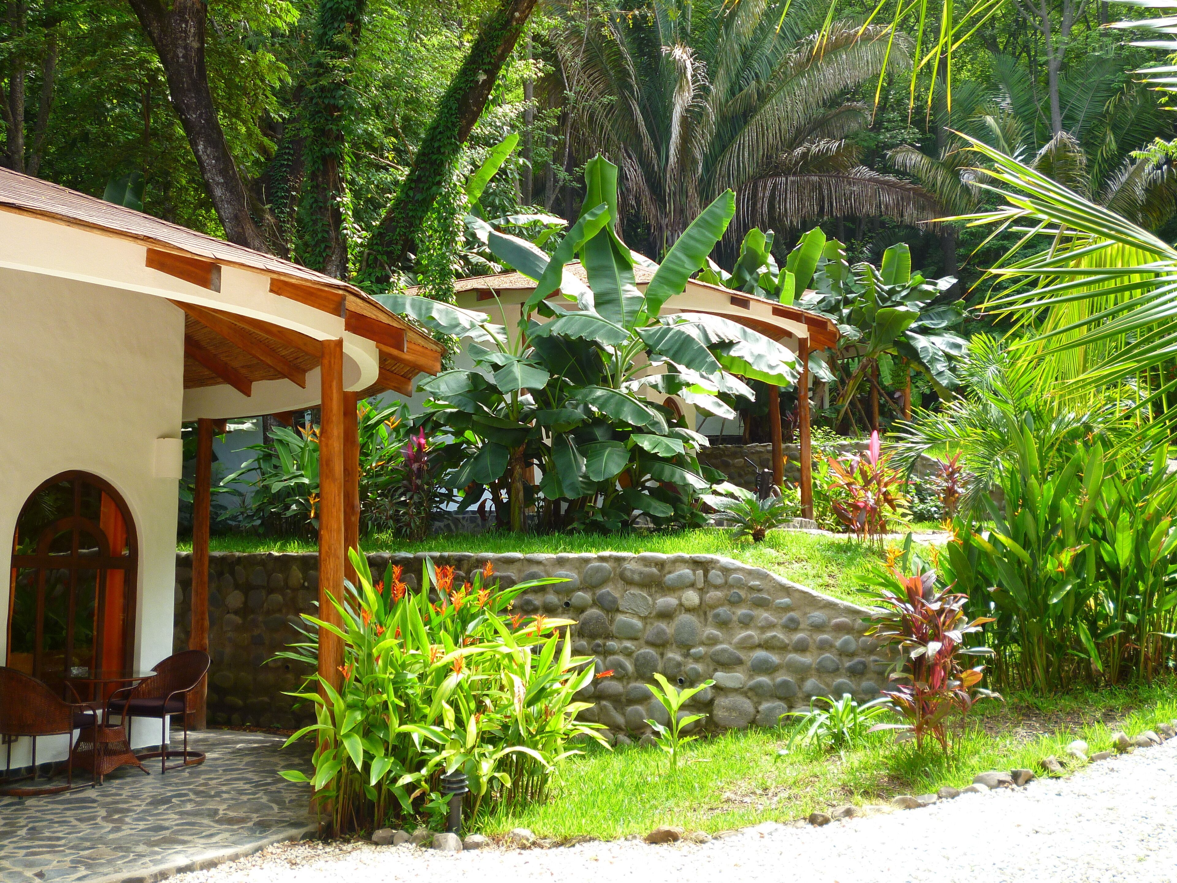 Um jardim com um muro de pedra, uma pérgula de madeira e uma área de estar com cadeiras.