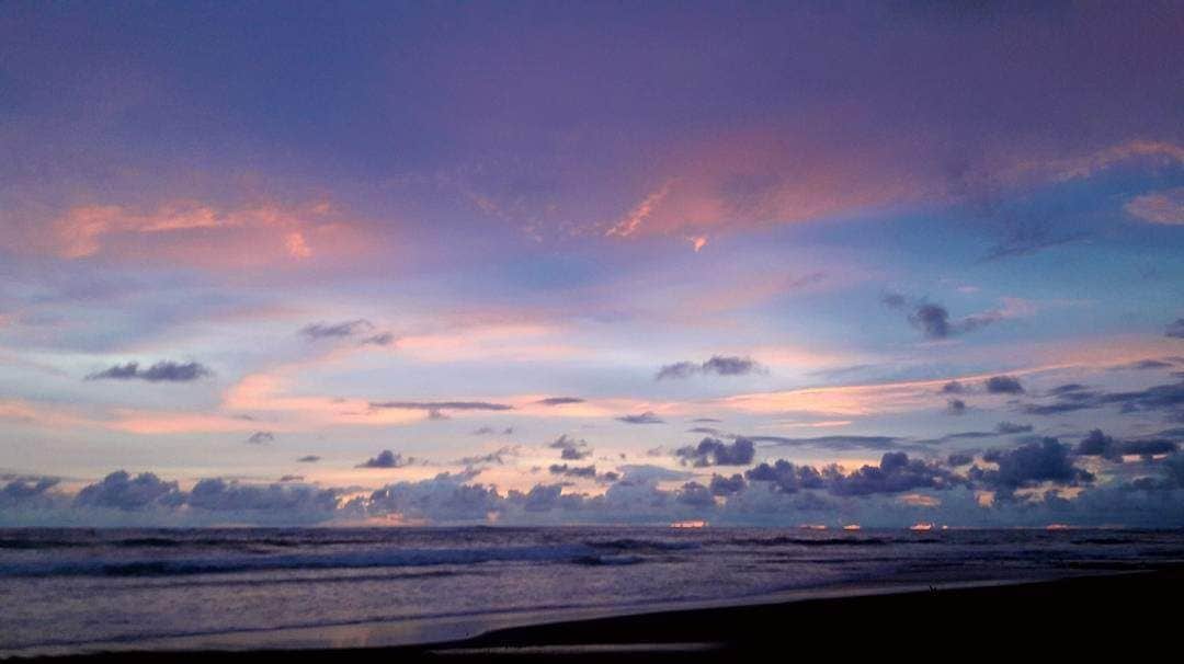 Cena de praia com céu ao pôr do sol e ondas.