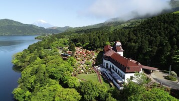 Um edifício grande e branco com telhado vermelho, rodeado por vegetação exuberante e um lago.