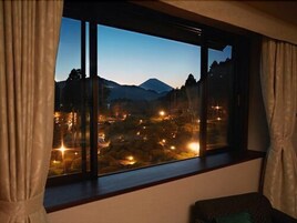 Quarto com uma grande janela com vista para uma paisagem montanhosa ao entardecer.