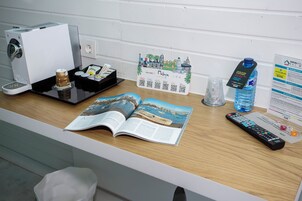 Um balcão com uma máquina de café, um controle remoto, uma revista, uma garrafa de água e um cartão de boas-vindas.