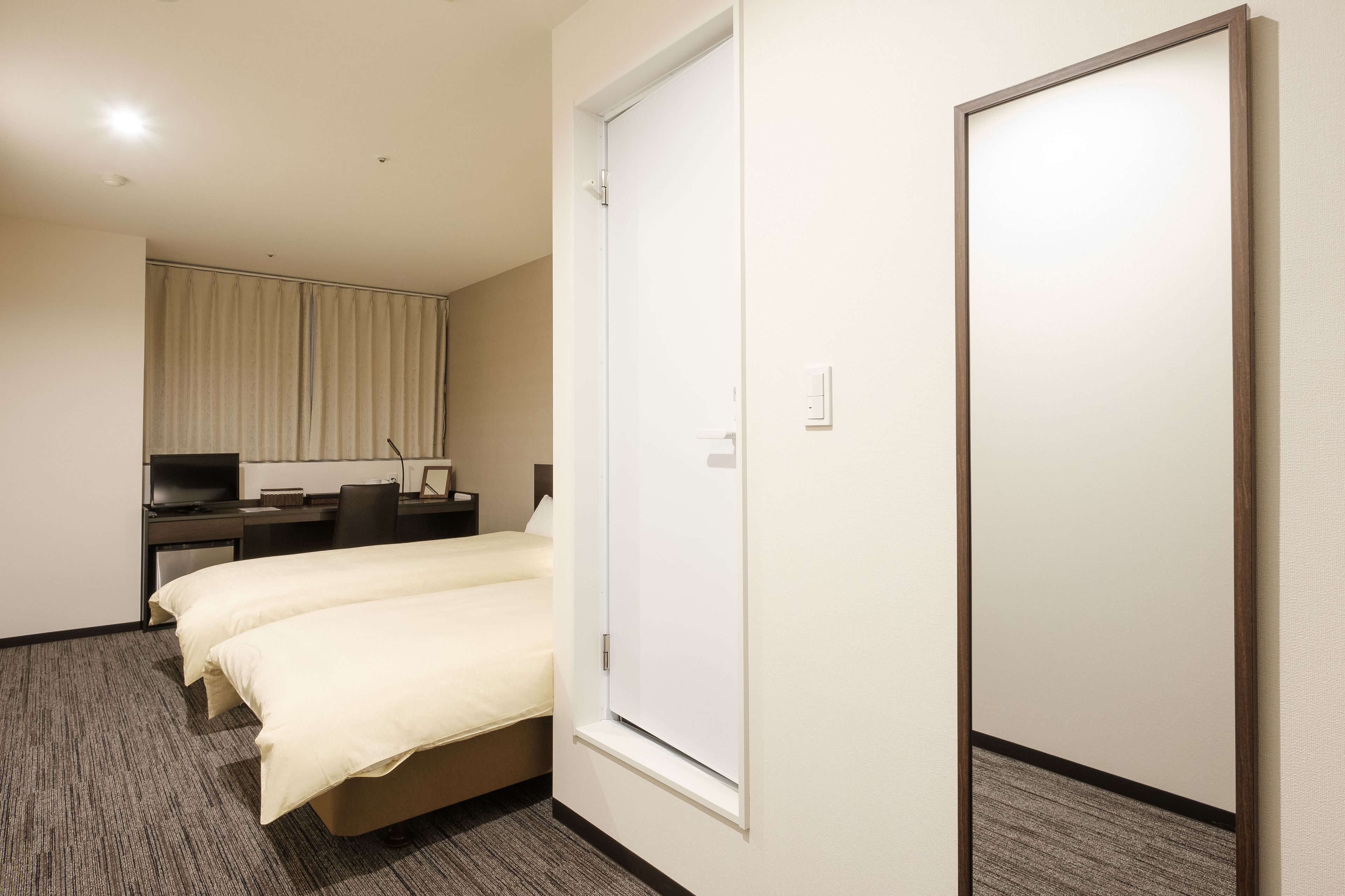 Quarto de hotel com duas camas, uma escrivaninha, uma cadeira, uma televisão e um guarda-roupa.
