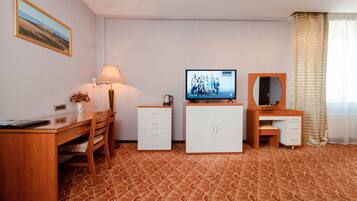 Quarto de hotel com secretária de madeira, televisão, guarda-roupa e espelho.