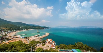Uma cidade costeira com praia, um cais e montanhas ao fundo.